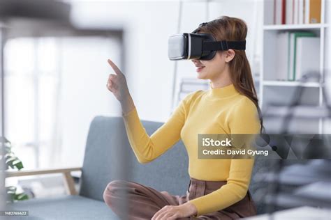 Vr 헤드셋을 착용한 젊은 라틴계 또는 아시아계 여성이 공기를 만지고 집에서 소파에 앉아 Vr 안경을 쓰고 웃고 있는 백인 여성 3차원 형태에 대한 스톡 사진 및 기타