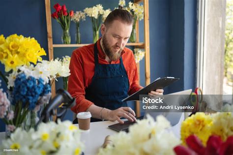 작은 꽃가게에서 앞치마를 두르고 노트북 컴퓨터와 클립보드를 사용하여 주문 세부 정보를 제공하는 백인 사업가 직장에서 남성 플로리스트 자영업자 꽃집 주인에 대한 스톡 사진 및