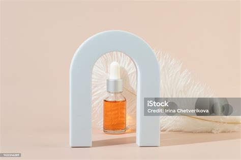 베이지 색 배경의 분홍색 깃털 앞에있는 아치에 서있는 오렌지색 네일 큐티클 오일이있는 점적기 병 0명에 대한 스톡 사진 및 기타 이미지 Istock