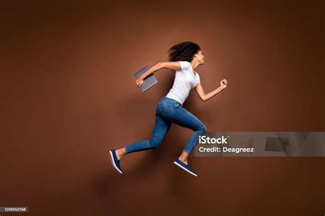 전체 길이 프로필 사진 재미 어두운 피부 여자 점프 높은 보유 노트북 서둘러 교실 착용 캐주얼 화이트 티셔츠 청바지 고립 된 갈색 색상 배경 T 셔츠에 대한 스톡 사진 및