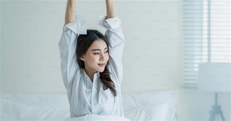 잠옷을 입은 아시아 아름다운 소녀는 아침에 행복으로 일어난다 매력적인 젊은 여성은 웃고 행복하고 긴장을 풀고 집 침실의 침대에서 잠에서 깨어난 후 몸을 스트레칭합니다