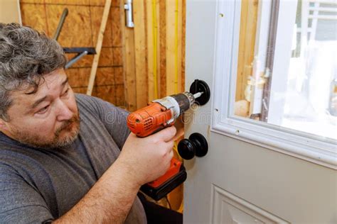 Man Installing A Door Handle Using A Power Drill In A Wooden Interior Setting During Daylight