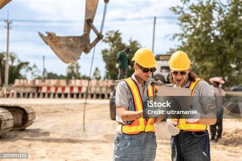 안전모와 안전조끼를 입은 두 명의 작업자가 굴삭기로 건설 현장에서 작업을 지시하며 팀워크 전략 계획 및 산업 조정을 강조합니다 2명에 대한 스톡 사진 및 기타 이미지
