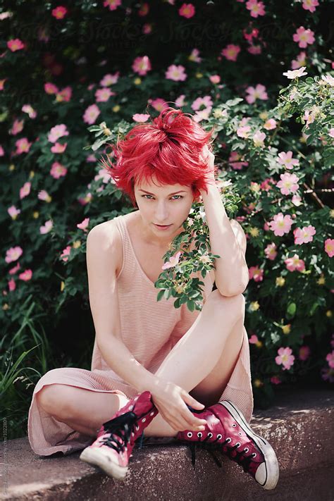 Caucasian Female With Bright Red Hair Sitting Near A Flowering Briar Bush By Stocksy