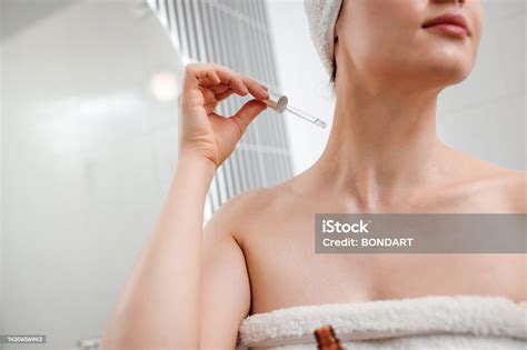 하얀 수건에 미용 제품이 들어간 작은 병을 들고 아침에 얼굴에 영양 노화 방지 보습 세럼을 바르는 인식 할 수없는 여성의 클로즈업 피부 관리 및 뷰티 컨셉 25 29세에