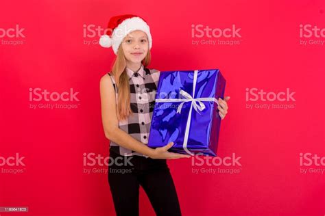 귀여운 어린 소녀는 크리스마스 모자를 입고 빨간색 배경 위에 고립 되어 서 현재 상자를 들고 겨울에 대한 스톡 사진 및 기타 이미지 Istock