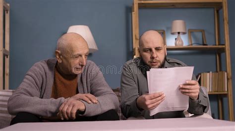 Elderly Father And His Adult Son Discussing Paper Documents Together At