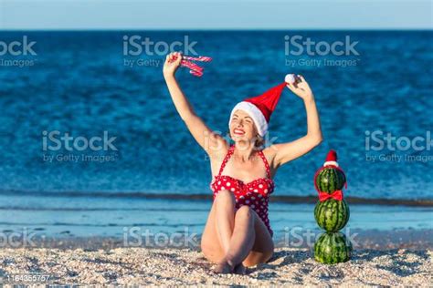 산타의 모자를 쓴 즐거운 젊은 여성이 크리스마스 사탕 지팡이를 들고 있고 수박 눈사람이 근처에 서 있습니다 겨울에 대한 스톡 사진 및 기타 이미지 Istock