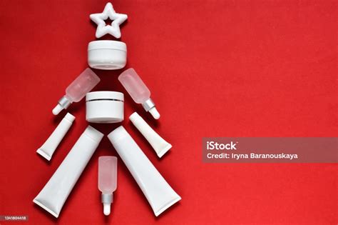 창조적 인 구성 붉은 배경에 크리스마스 트리 모양의 모이스처라이저 크림 항아리와 세럼 병과 흰색 튜브 스킨 케어 화장품 공간을 복사합니다 맨 위 보기입니다 크리스마스 트리에