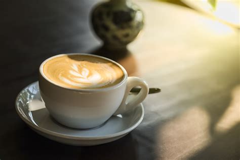 뜨거운 커피 라떼 화이트 컵에 우유 거품 아트와 접시와 숟가락을 아침 햇빛과 그림자가 있는 나무 테이블에 닫습니다 0명에 대한 스톡 사진 및 기타 이미지 Istock