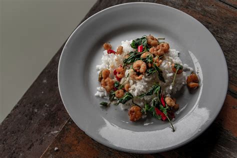 볶음 태국 바질과 난쟁이 새우를 얹은 쌀은 나무 테이블에 흰색 접시에 제공 태국 스타일의 음식 건강한 식생활에 대한 스톡 사진