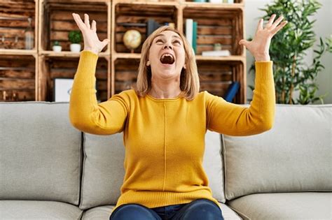 중년 백인 여성은 집에서 소파에 앉아 캐주얼 한 옷을 입고 미친 듯이 소리치고 공격적인 표정과 팔을 들고 소리쳤다 좌절 개념 함성에 대한 스톡 사진 및 기타 이미지 Istock