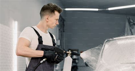 흐르는 물과 거품으로 세차 청소 거품으로 고압 스프레이를 들고 있는 젊은 세차 서비스 남성 직원의 측면 모습 세차장 역에 세탁기가 있습니다 사진 Unsplash의