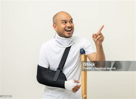 충격을 받은 얼굴 남자가 팔과 다리가 부러져 빈 공간을 가리키고 있다 남자는 지팡이 목발로 석고 캐스트 부목을 착용했습니다 목 칼라가 있는 슬링 지지 팔을 착용한 환자 생명