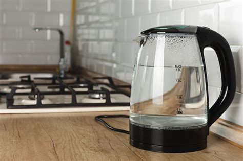 주방의 나무 테이블에 있는 현대적인 전기 투명 주전자 물을 끓이고 차를 만들기위한 주전자 뜨거운 음료를 만들기위한 가전 제품 복사 공간 텍스트를 위한 장소입니다 가정 생활에