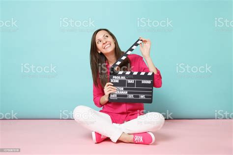 전체 길이 총된 여자 장미 셔츠 화이트에서 바지 만들기 Clapperboard 밝은 핑크 블루 파스텔 벽 배경 스튜디오에 절연 필름으로 바닥에 앉아 복사 공간을 조롱 하는