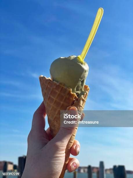헤이즐넛과 피스타치오 젤라토 노란색 플라스틱 아이스크림 숟가락이 들어 있는 와플 콘을 들고 있는 알아볼 수 없는 사람의 클로즈업 이미지 화창한 날에 베니스 해안가를 걷고