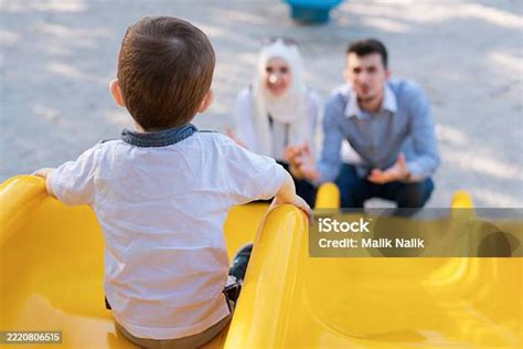 행복한 무슬림 가족이 공원 놀이터에서 함께 놀고 있고 엄마와 아빠는 미끄럼틀에서 내려오는 아이를 팔을 뻗고 기다리고 있습니다 3 명에 대한 스톡 사진 및 기타 이미지