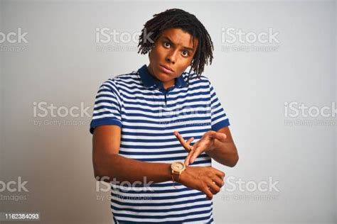 고립 된 흰색 배경 위에 서있는 줄무늬 파란색 폴로를 입은 공포를 가진 아프로 남자 시간 조바심 화가 및 마감 지연에 대한 화가 를 가리키는 서둘러 가리키기에 대한 스톡