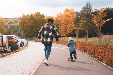 다른 도움 그녀의 아들은 킥 스쿠터와 함께 타고 행복한 가족 어머니는 아이 아들에게 공원에서 스쿠터를 타도록 가르칩니다 어린 시절의 부모 역할 아이디어를 지원하십시오 행복한