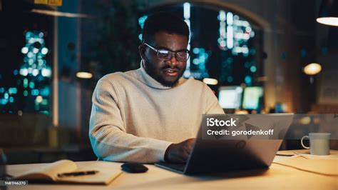 저녁 시간 동안 사무실에서 노트북 컴퓨터에서 일하는 약간 동요 된 남성 직원 다양한 흑인 아프리카 전문가 인터넷 검색 금융 데이터 조사 직장 이메일에 응답 걱정하는에 대한