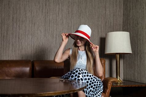 빈티지 인테리어 거실에서 핀업 스타일의 드레스 물방울 점과 모자를 쓴 초상화 중년 여성 카메라를 보는 여성 복고풍 스타일링 옷을