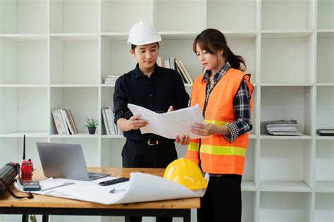 Engineers Collaboration On Construction Project In Modern Office With Blueprints And Safety Gear