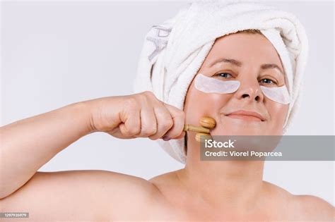 깨끗한 피부와 머리띠 붕대를 가진 노인 여성이 카메라를 바라보며 나무 롤러 마사지기로 오토마사지를 합니다 흰색 배경입니다 사람 얼굴에 대한 스톡 사진 및 기타 이미지
