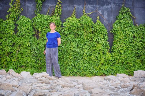 녹색 잎의 벽 배경에 소녀 복사 공간 돌 바닥 크리퍼의 벽과 안경을 쓴 젊은 여성 파란 옷을 입은 아름다운 여성이 여름 풍경에 맞서 완전히 성장합니다 갈색 머리에 대한 스톡