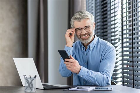 노트북과 메모장이 있는 현대 사무실에서 스마트폰을 사용하는 웃는 사업가 Brand Name Smart Phone에 대한 스톡 사진 및 기타 이미지 Brand Name