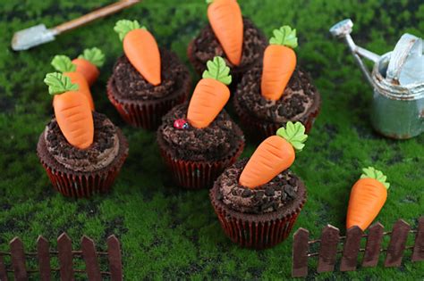 초콜릿 파이프 아이싱 프로스팅 초콜릿 뿌리 오렌지 퐁당 당근 모델 급수 캔과 울타리 종이 케이크 케이스 푸른 하늘과 녹색 잔디 배경 높은 전망 전경에 초점을 얹은 홈메이드