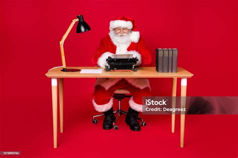 산타 클로스 회색 수염 앉아 테이블 작업 타자기 램프 책 착용 X마스 의상 코트 모자 사양 안경 격리 된 빨간 색 배경의 전체 길이 사진 남자에 대한 스톡 사진 및 기타