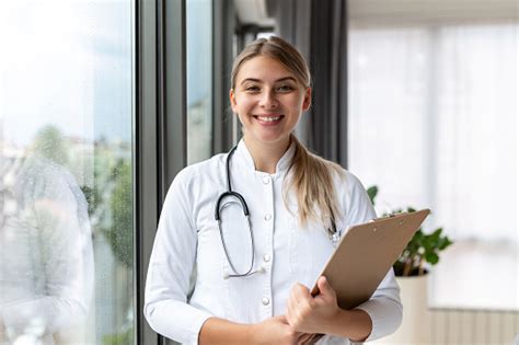 자신감 넘치는 미소 짓는 의사가 포즈를 취하고 청진기로 카메라를 바라 봅니다 친절한 여성 의사가 웃고 있습니다 목에 청진기를 착용한 의사 경영자에 대한 스톡 사진 및 기타