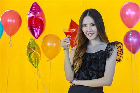 노란색 벽과 색상 전체 풍선 파티와 레드 와인 잔을 들고 미소 아름다운 젊은 아시아 여성의 초상화 휴일 시즌과 새해 또는 크리스마스 사진 공휴일에 대한 스톡 사진 및 기타