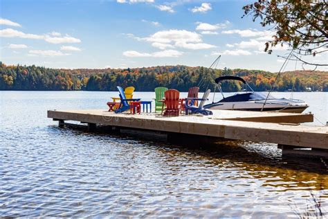 Colourful Adirondack Chairs On A Wooden Pier On A Lake A Boat Is Tied