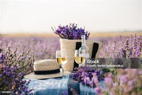 라벤더 밭의 배경에 화이트 와인과 병이 든 두 잔 피크닉에서 담요에 꽃 라벤더가있는 밀짚 모자와 바구니 일몰 광선에서 낭만적 인 저녁 프로방스의 여름 프랑스 와인에 대한