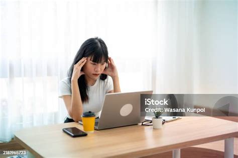 노트북 화면을 보며 스마트폰과 책상 위의 커피로 스트레스와 걱정을 표현하는 걱정스러운 아시아 여성 Brand Name Smart