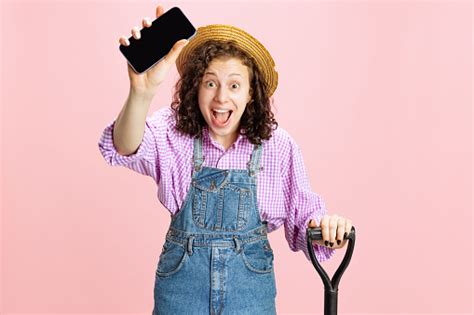 젊은 행복한 소녀 작업 유니폼과 분홍색 배경에 고립 된 전화를 사용하여 모자를 쓴 여성 정원사 직업 감정 농약 에코의 개념 20 24세에 대한 스톡 사진 및 기타 이미지
