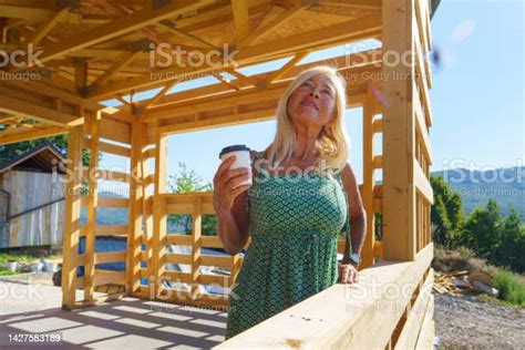 커피와 함께 서서 멀리 바라 보는 행복한 노인 여성 그녀의 새로운 미완성 생태 목조 주택의 옥외 Diy에 대한 스톡 사진 및 기타 이미지 Istock