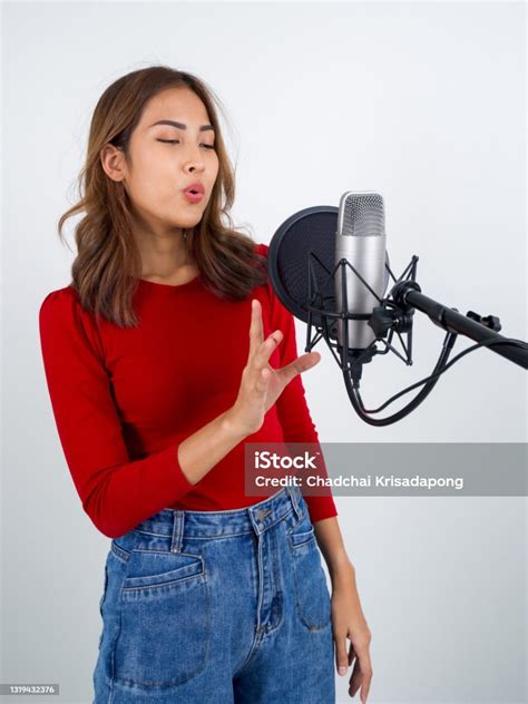 빨간 긴 소매 티셔츠를 입은 젊은 아시아 여성이 흰색 벽 앞에서 마이크와 함께 노래하고 있습니다 전문 녹음 스튜디오에서 음악을 생산하는 뮤지션 가수에 대한 스톡 사진 및