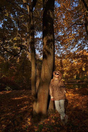 밝은 노란색과 빨간색 단풍이 있는 나무가 있는 가을 공원의 나무 줄기에 기대어 햇살을 쬐며 모자를 쓴 아름다운 젊은 여자 10월에 대한 스톡 사진 및 기타 이미지 Istock