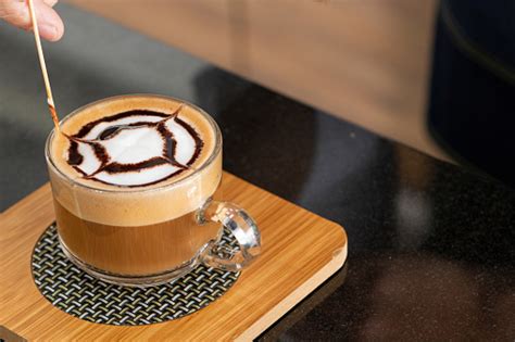 카페 가게에서 뜨거운 커피 한 잔을 들고 바리스타의 손 바리스타는 커피 한 잔을 들고 검은 커피를 마시며 현대 커피숍의 카운터 뒤에 서 있습니다 어린 바리스타가 미소를