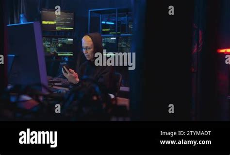 Female Caucasian Hacker Sitting In Front Of Big Screen And Tapping Or Texting Message On Phone