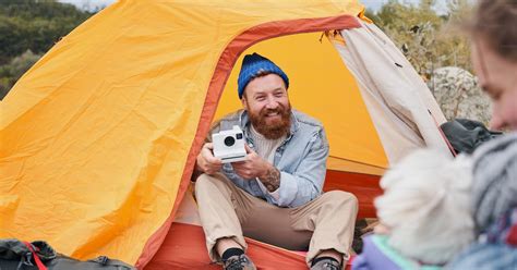 잘 생긴 수염 난 남자는 텐트에 앉아있는 동안 그녀의 팔에 개를 안고 사랑하는 여성의 폴라로이드에 미소 짓고 사진을 찍는다 사진 Unsplash의 텐트 이미지