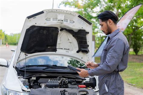 자동차 정비사는 클립보드에 체크리스트를 검사하고 작성하여 자동차를 검사합니다 정비공은 길가에 고장난 자동차와 함께 노트북 컴퓨터에서 자동차 부품 재고를 확인합니다 30 34