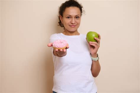 신선한 녹색 사과와 뿌려진 분홍색 도넛을 들고 있는 여성은 건강에 좋은 음식과 단 음식 사이의 선택을 나타냅니다 40 44세에 대한 스톡 사진 및 기타 이미지 Istock