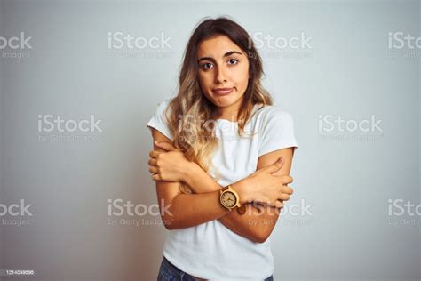 젊은 아름다운 여자는 얼굴에 슬프고 충격 표정으로 겨울 추위에 대한 고립 된 배경 흔들림과 동결 위에 캐주얼 흰색 티셔츠를 입고