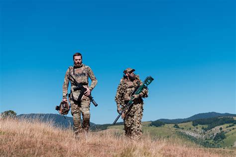 저격수 팀 병사 분대가 잠복하고 있습니다 스나이퍼 조수이자 팀 리더는 노란 잔디와 푸른 하늘로 자연을 걷고 목표로합니다 전술 위장 유니폼 2명에 대한 스톡 사진 및 기타