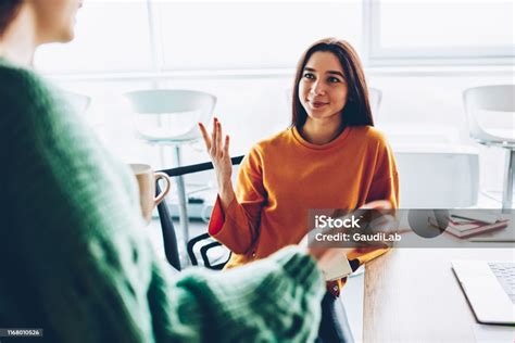 갈색 머리를 가진 아름다운 여성 디자이너는 대학에서 바탕 화면에 앉아 휴식 하는 동안 동료에 게 새로운 창조적인 아이디어를 설명 매력적인 젊은 여자 옷을 입고 캐주얼 착용