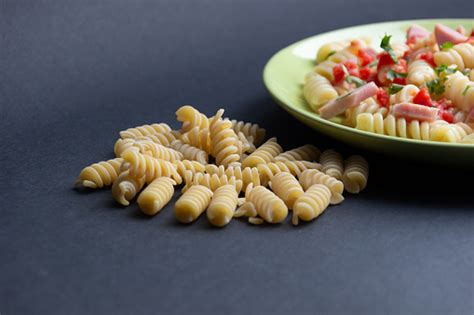 토마토 베이컨 치즈 녹색 접시에 포크와 나이프 검은 색 배경에 건조 마카로니를 곁들인 뜨거운 푸실리 파스타 건강한 생활방식에